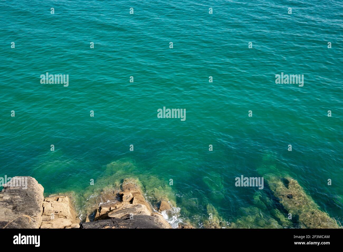 Looking down to rocks and blue pristine sea. Ocean background with copy ...