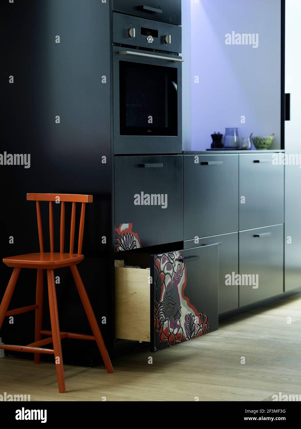Wooden chair in front of black kitchen unit with large drawers and oven ...