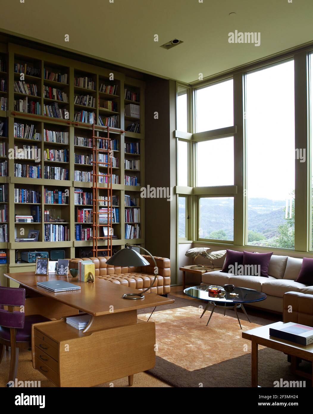Bookcase in study with high ceiling and uncurtained windows, California ...