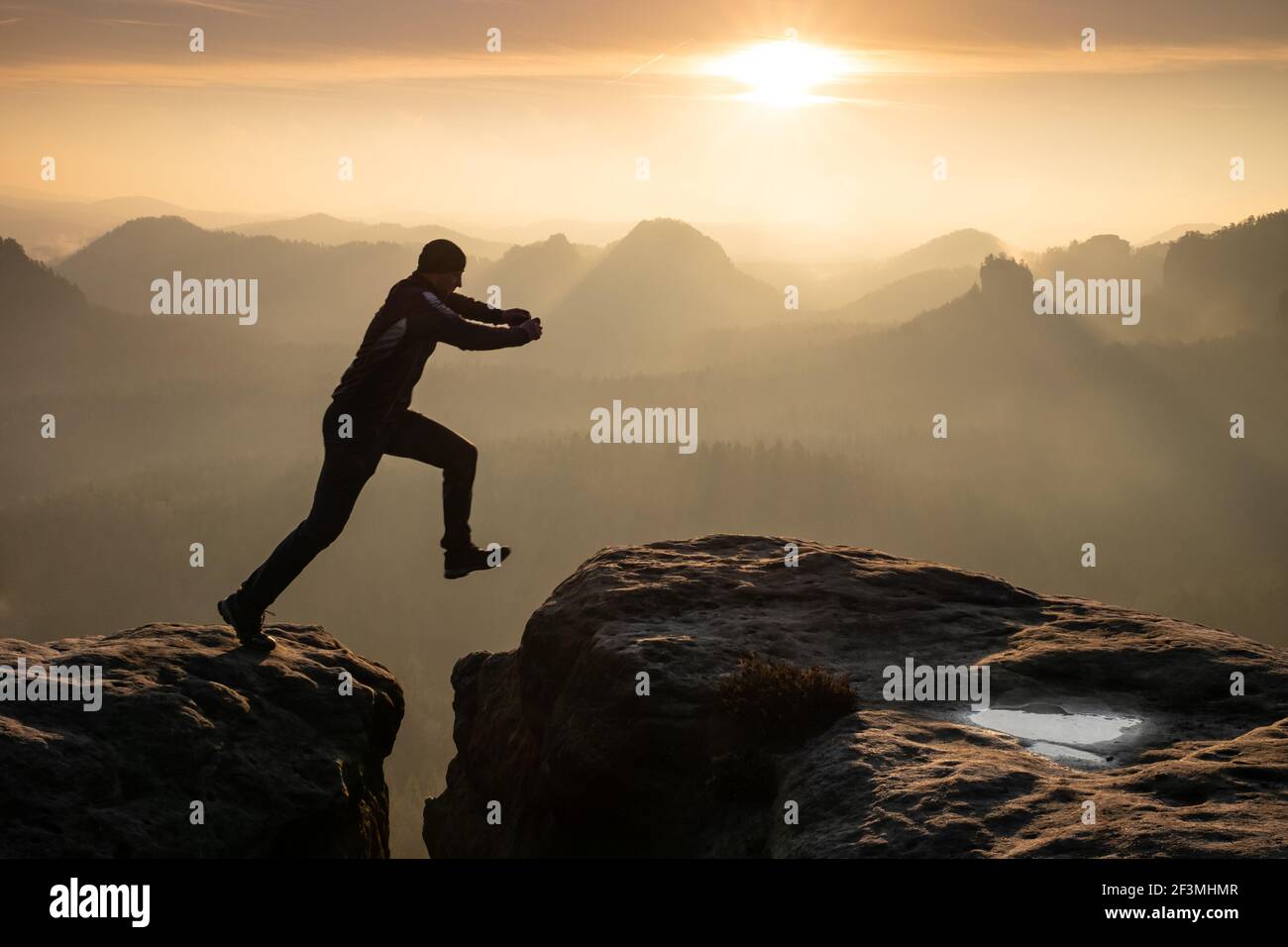 Strong mountain climber hiking and jumping over the summit ridge of a ...