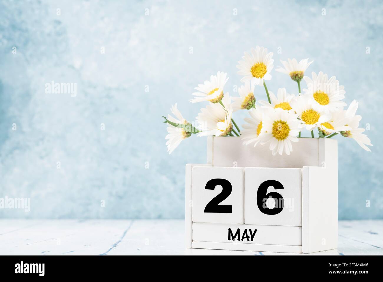 White cube calendar for May decorated with daisy flowers over blue ...