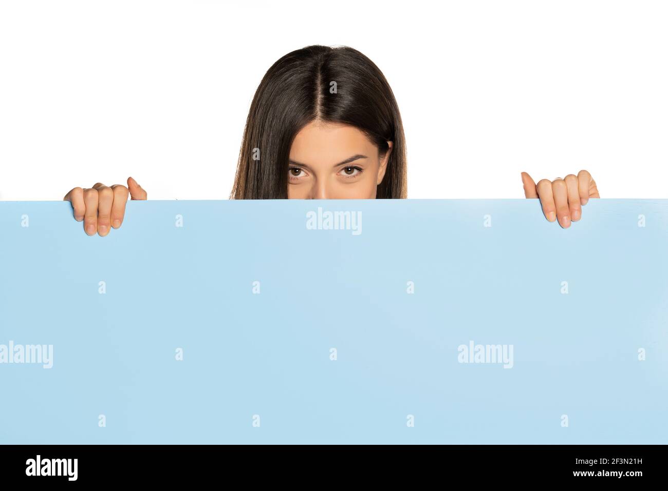 young beautiful woman peeking behind a blue empty board on white ...