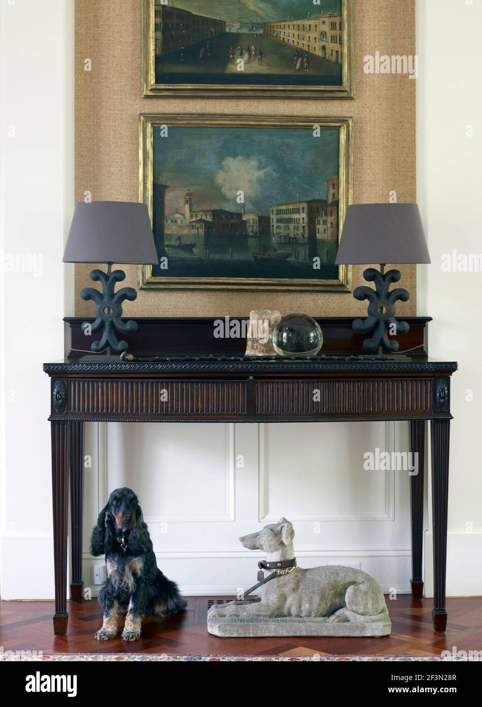 Dog sits with dog sculpture below console in traditional US home Stock ...