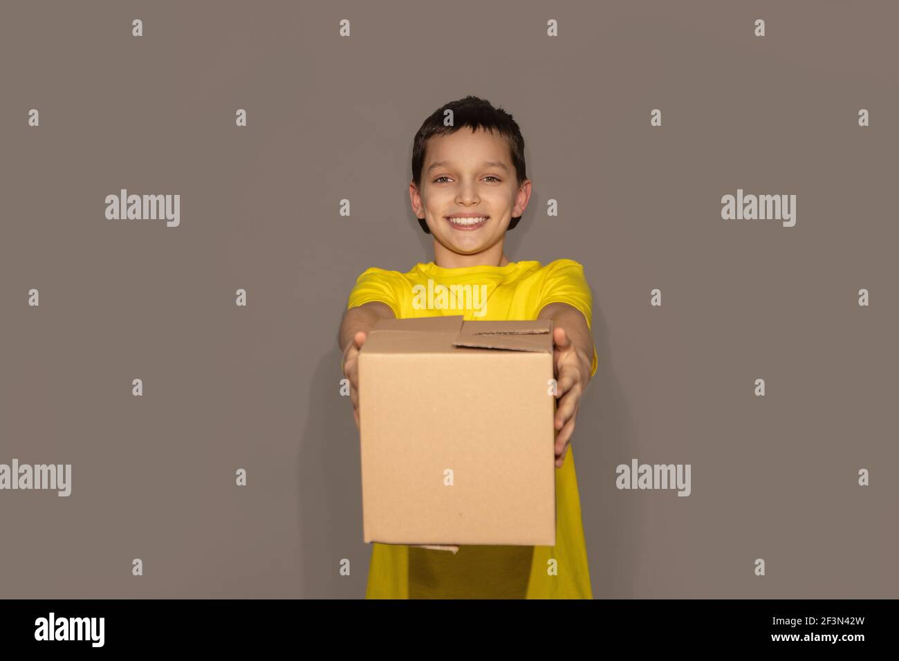 Smiling young delivery teen boy holding and carrying a cardboard box ...