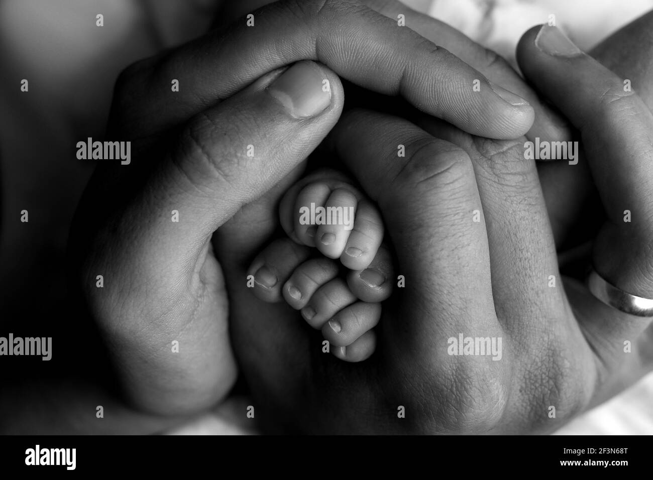 Father's caring hands hold the little feet of the newborn on a black ...