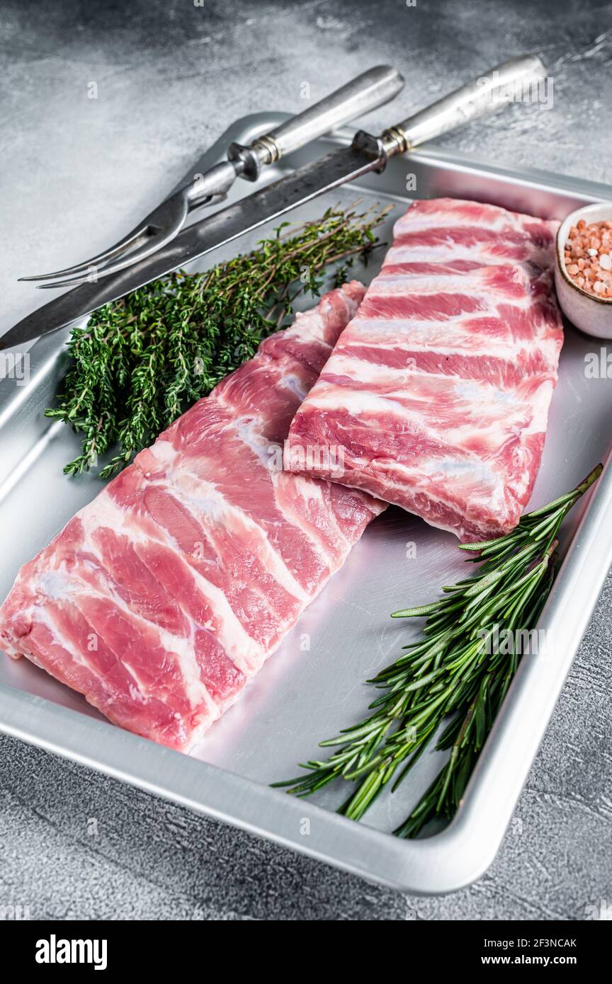 Rack of Raw pork spare ribs in kitchen oven tray with herbs. White ...