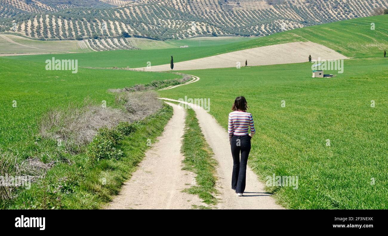 Young short hair brunette woman seen from behind walking on a path in ...