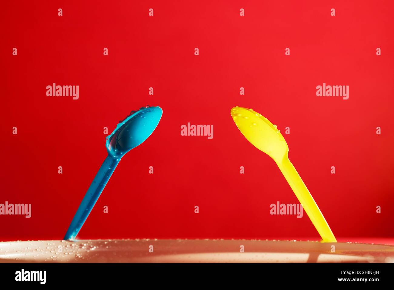 yellow and blue plastic spoonfuls on a red background Stock Photo - Alamy