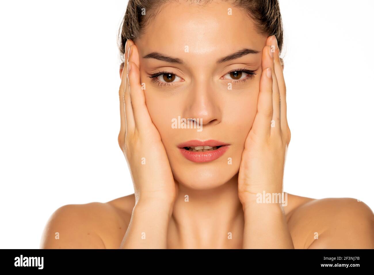 a young beautiful woman tightens her face with her hands on white ...