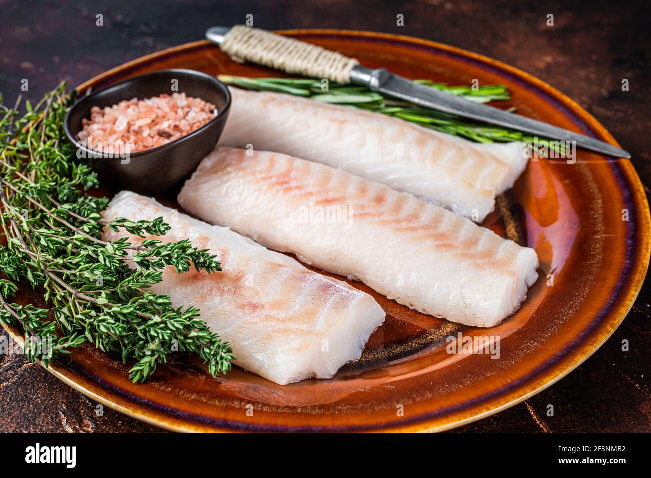 Raw cod loin fillet steaks on rustic plate with thyme and salt. Dark ...