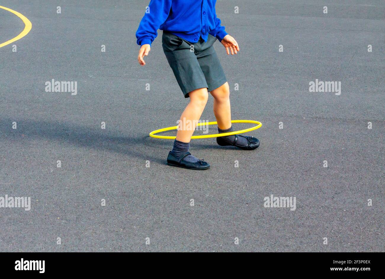 Primary school child playing with a hoop outside in a school playground ...