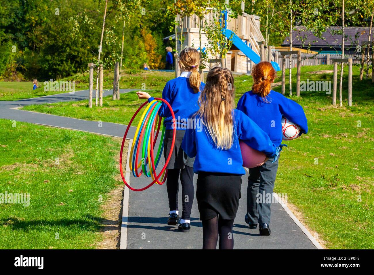 Group of three primary schoolgirls with blue uniform tops carrying ...