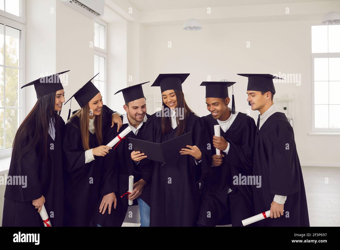 Students of different nationalities in graduation gowns look at photos ...