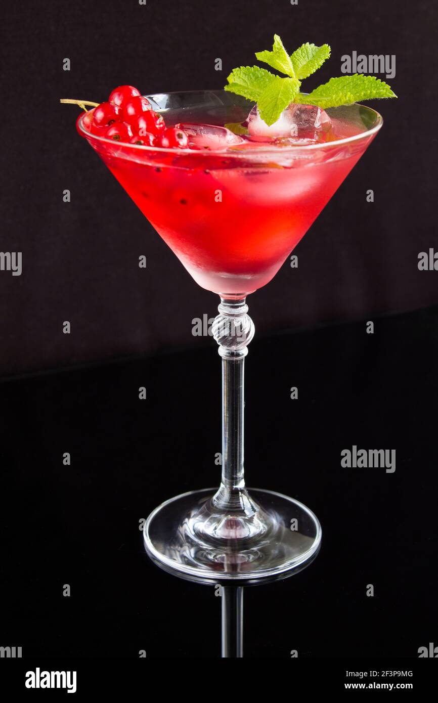 Cold cocktail with red currants in the martini glass on the black ...