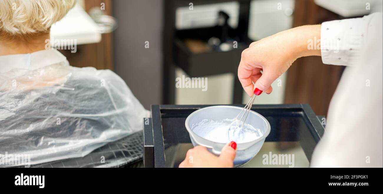 The hairstylist makes a white color dye mix for coloring hair at a ...