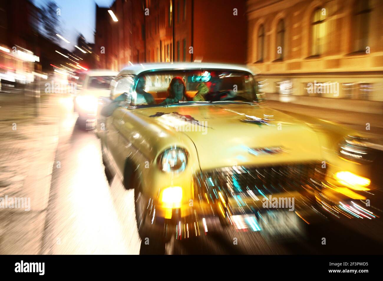 Car parade with American vintage cars through a city one evening in ...