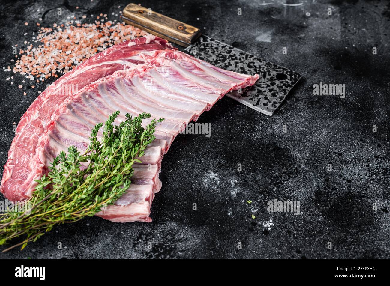 Raw rack of lamb ribs on butcher cutting board with herbs. Black ...