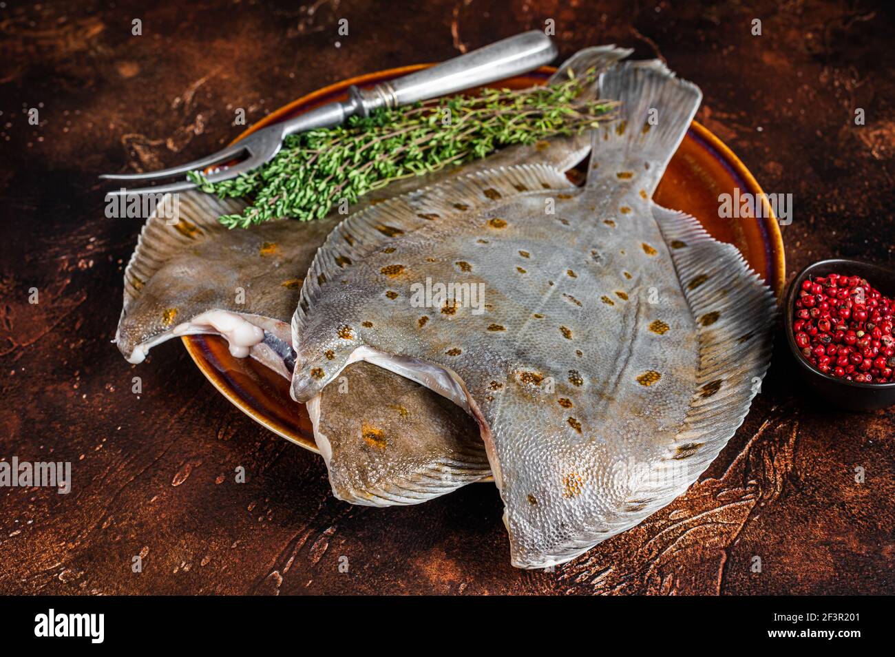Raw flounder or plaice on rustic plate with herbs. Dark background. Top ...