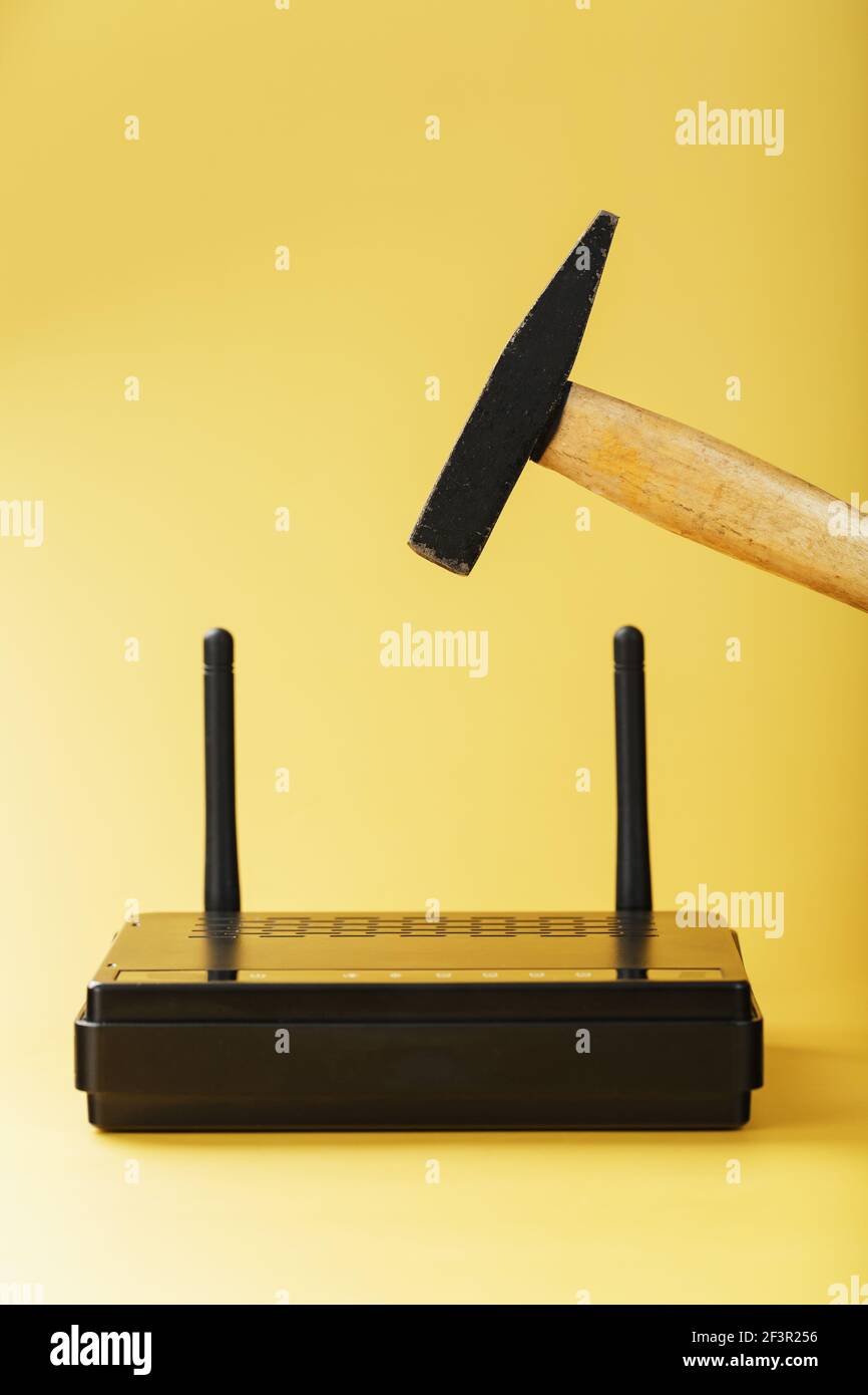 A hammer hits the Wi-Fi modem router to break it against a yellow ...