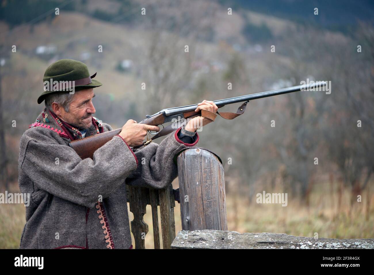 A hunter with a gun in his hands in hunting clothes takes aim and is ...