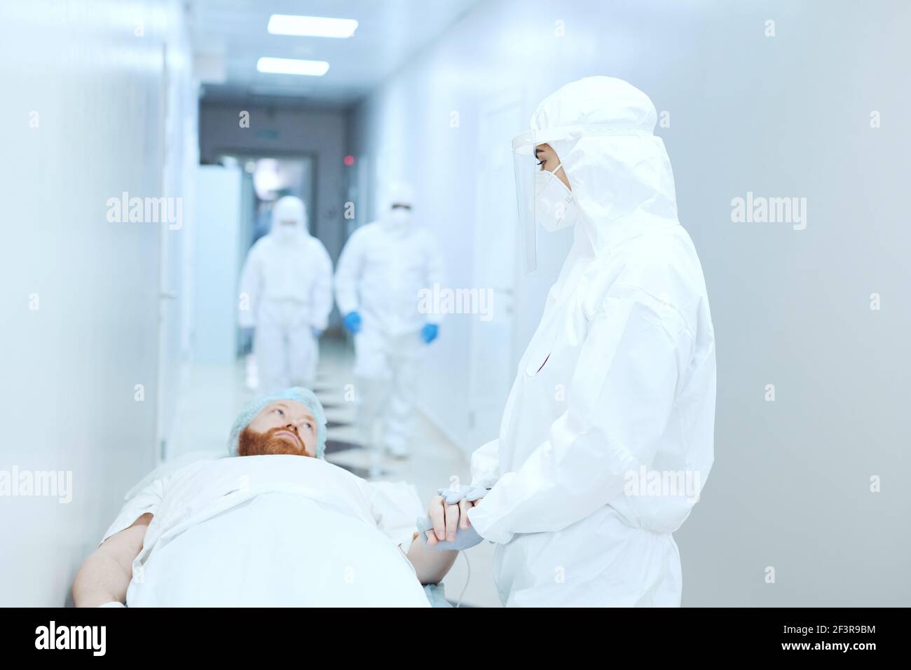 Doctor in protective uniform holding hands of the patient and talking ...