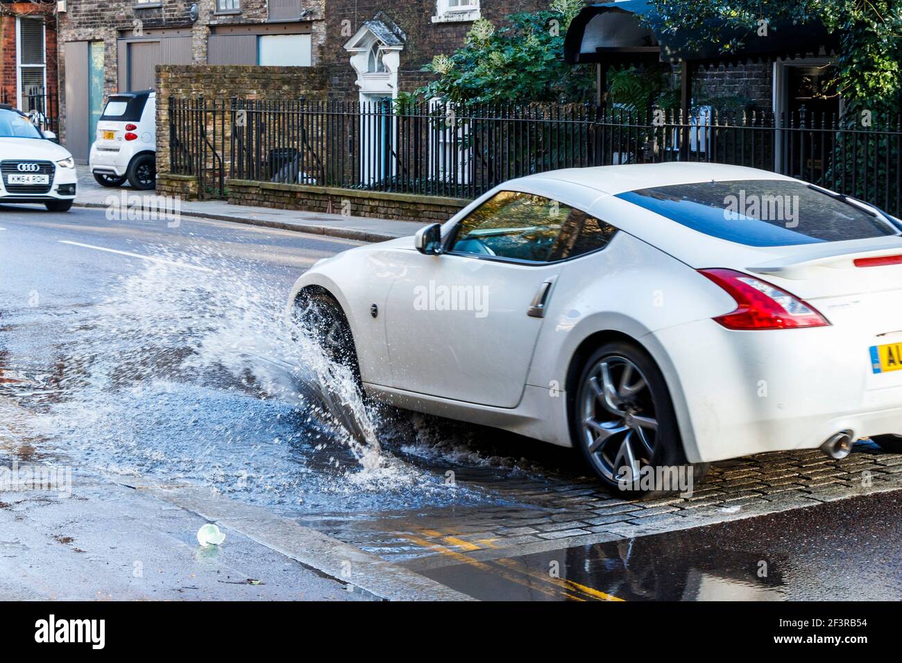 A car drives through a large roadside puddle caused by a mains water ...