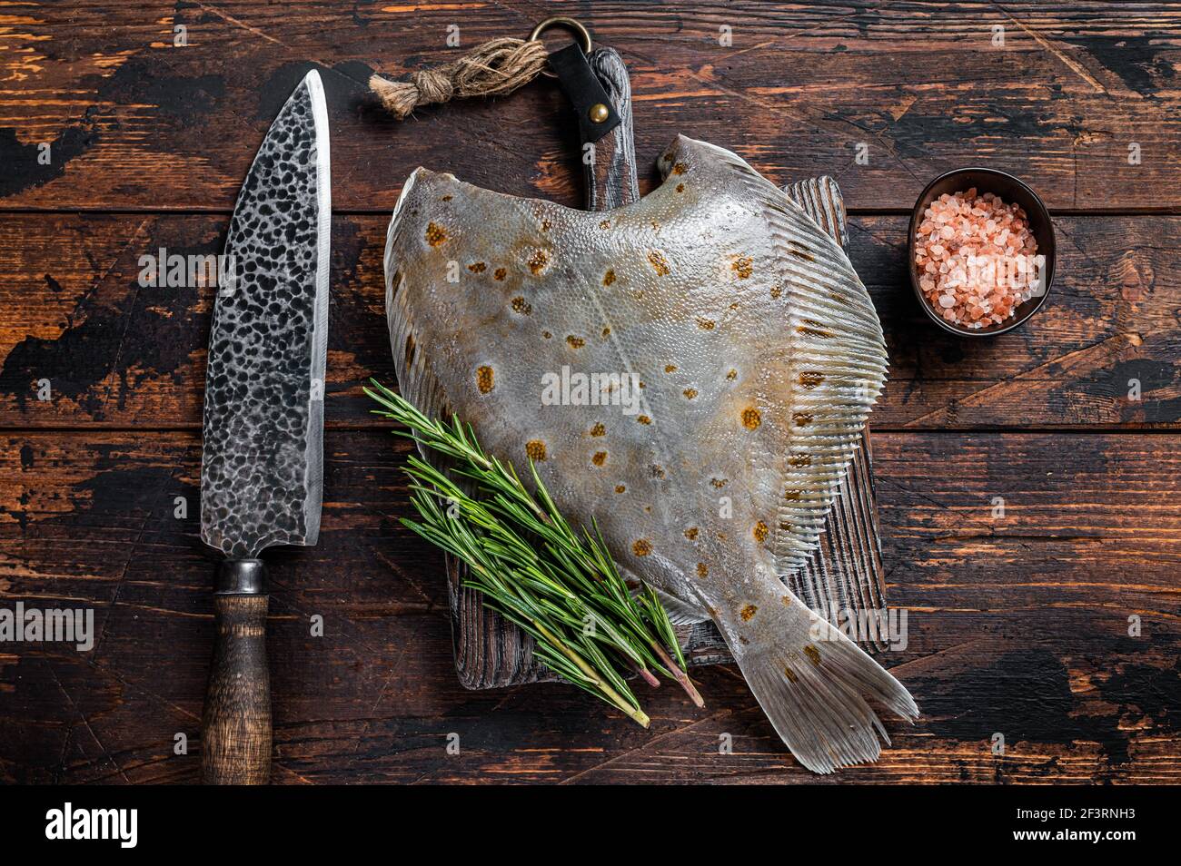 Raw plaice flatfish fish on butcher board with knife. Dark wooden ...