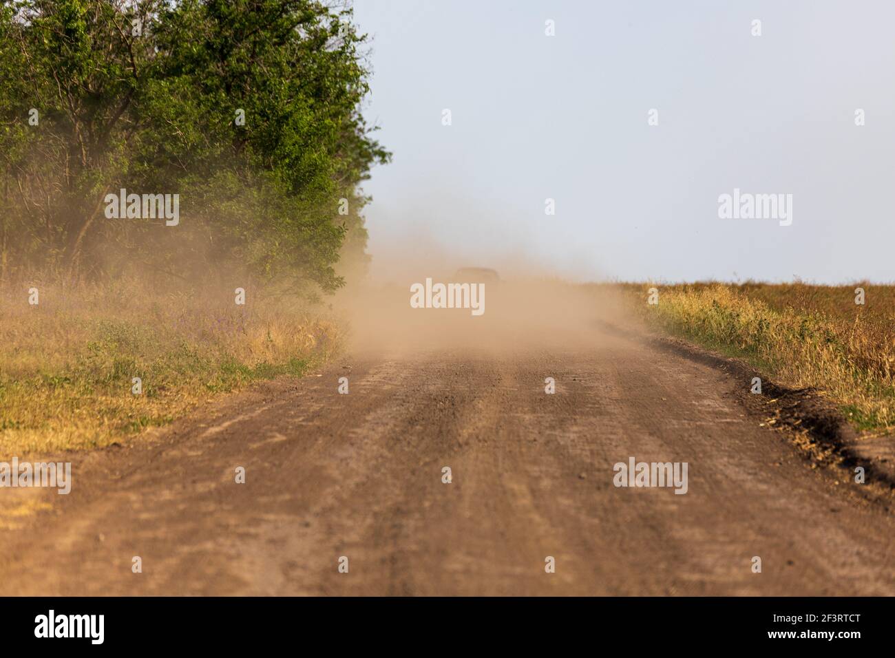 A car in a cloud of dust, driving off into the distance along a rural ...