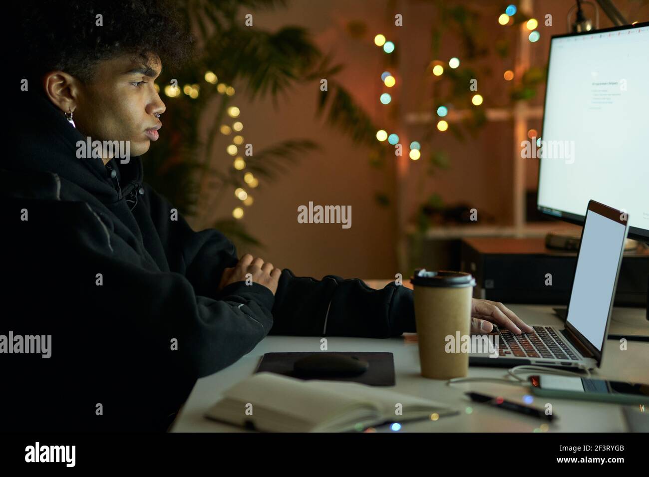 Side view of stylish young guy looking at monitor screen while working ...