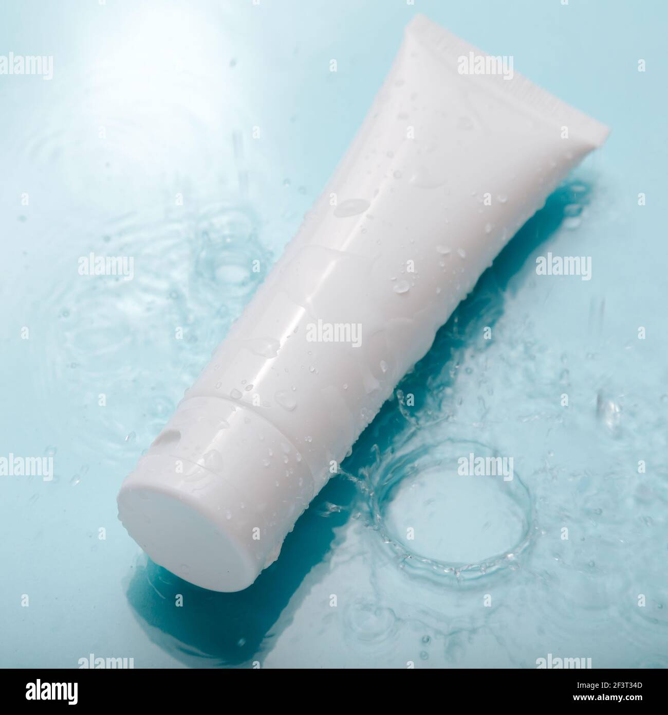 White cosmetic product in tube on color blue background with water ...