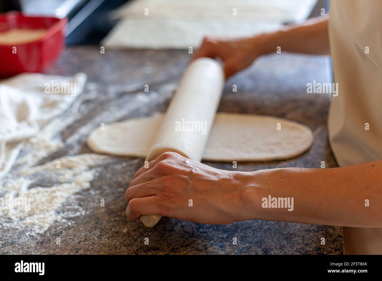 A caucasian woman is using an American rolling pin to roll over bread ...
