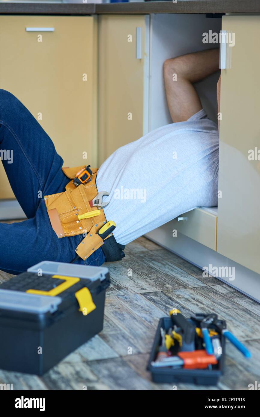 Get fixed. Professional plumber wearing tool belt examining and fixing ...