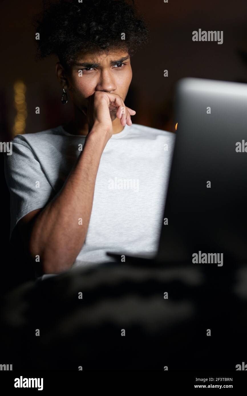 Night portrait of focused young guy looking tense at the screen ...