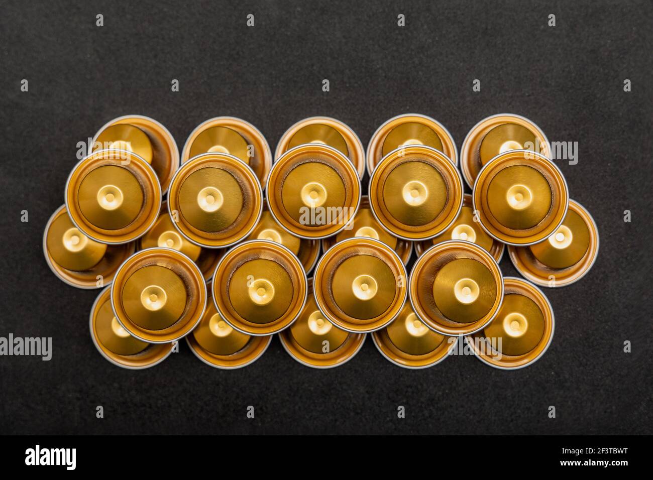 Construction of golden coffee capsules stacked on a dark background ...