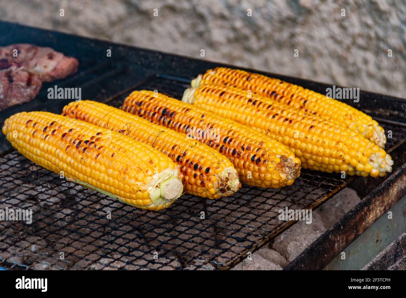 yellow ripe juicy cobs of corn lie on an iron grill next to meat that ...