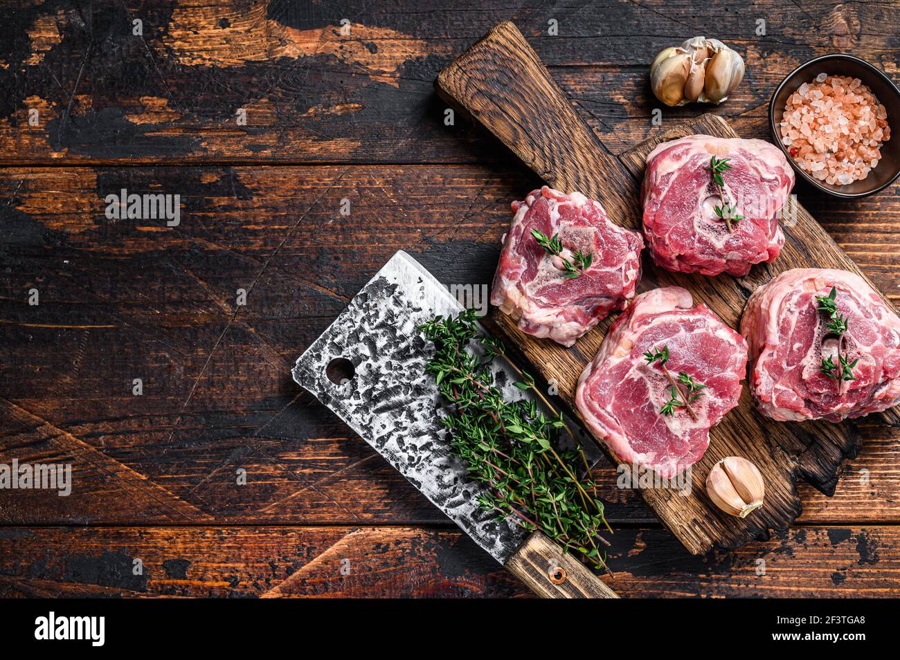 Raw mutton lamb neck meat on a butcher board with cleaver. Dark wooden ...