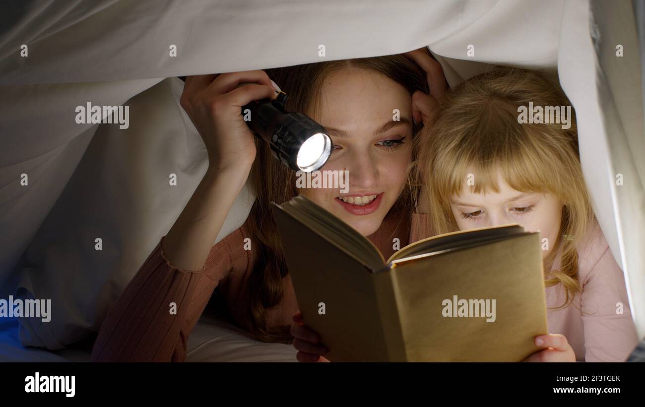 Young mother reading goodnight story fairytale to child daughter under ...