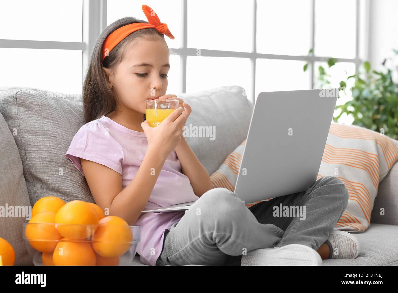 Cute little girl with orange juice and laptop on sofa in room Stock ...