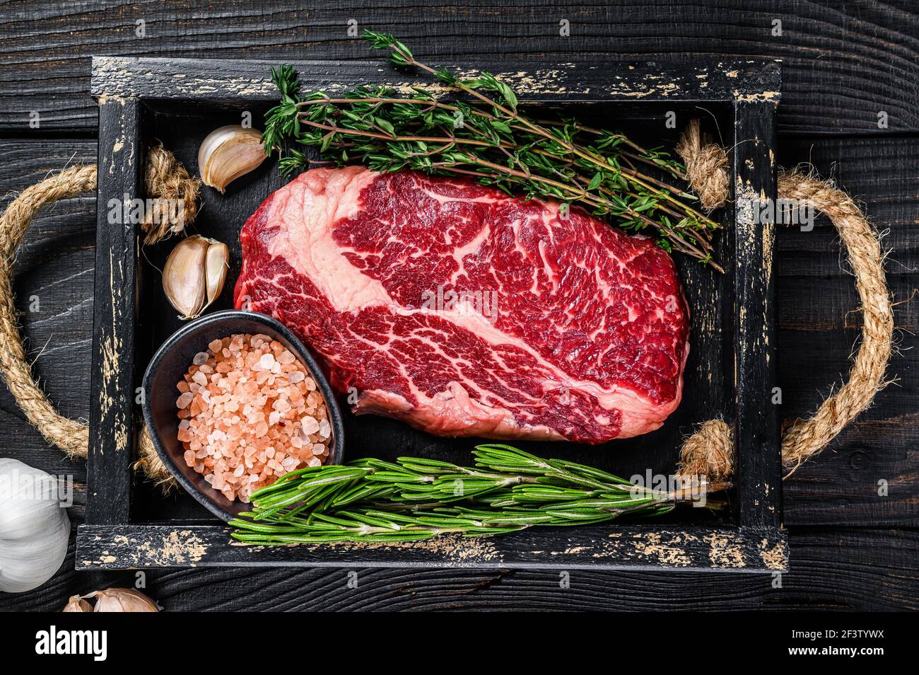 Raw prime rib eye beef meat steak in a butcher wooden tray with herbs ...