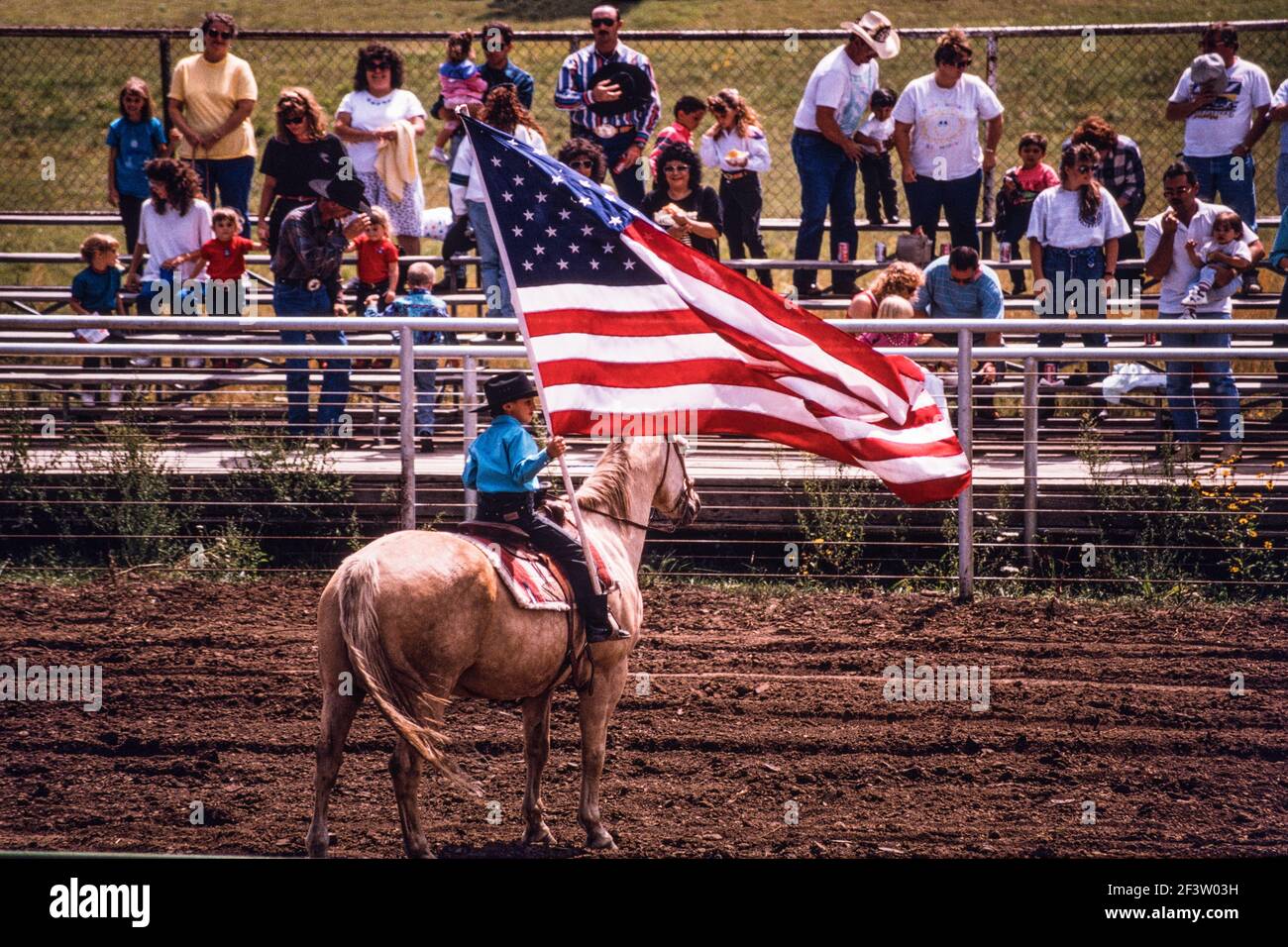 A young cowgirl riding her horse presents the American flag at the ...