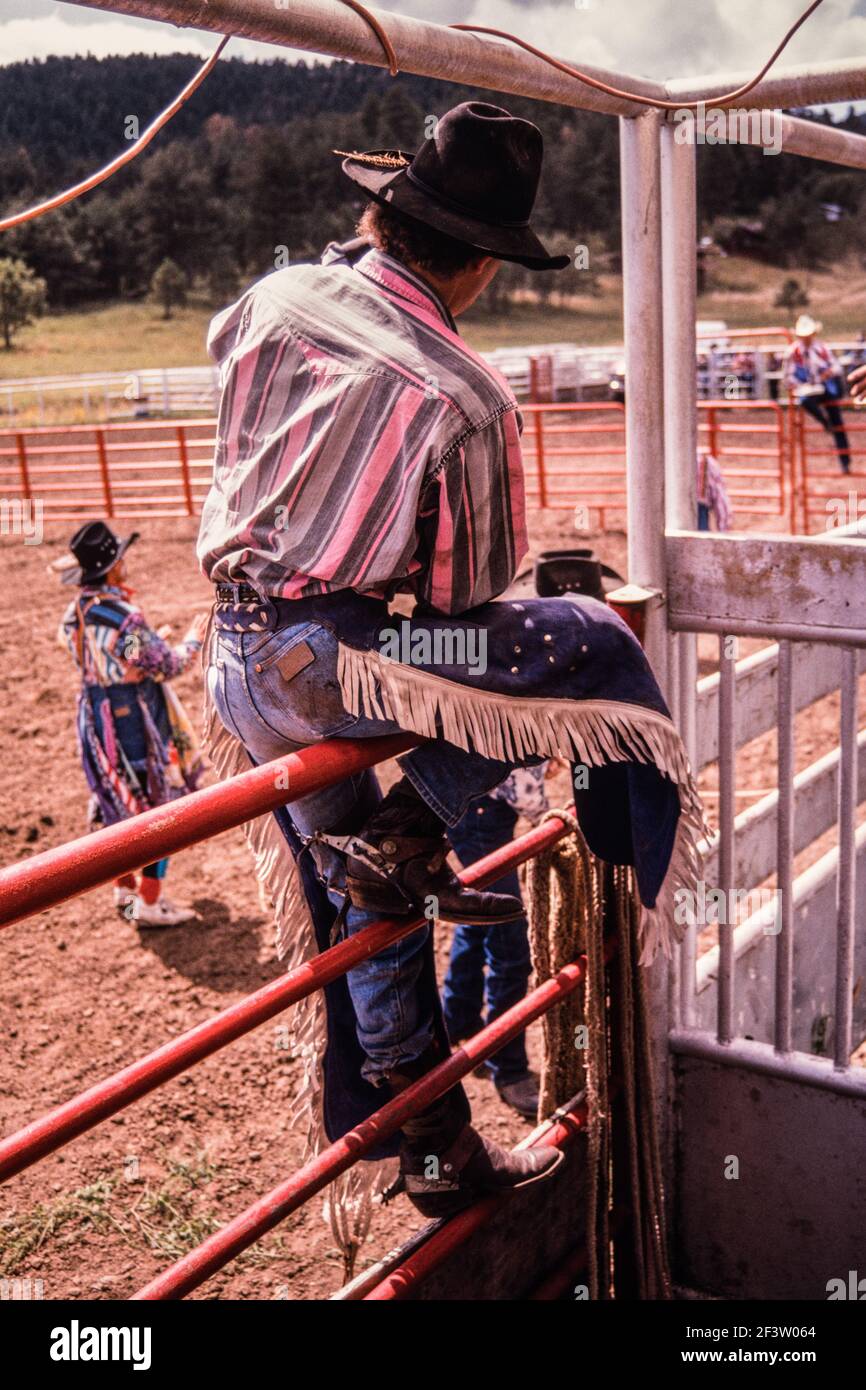 A cowboy competing in the bull-riding event waits on the arena fence in ...