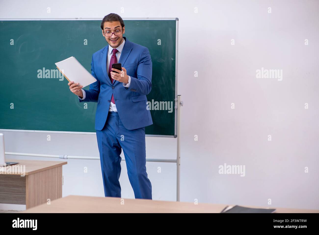 Young teacher in suit in front of green board Stock Photo - Alamy