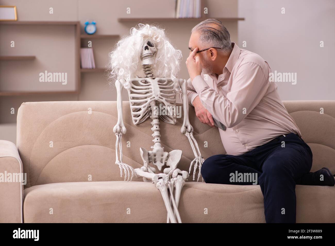 Old man sitting on the sofa with the female skeleton in undying love ...
