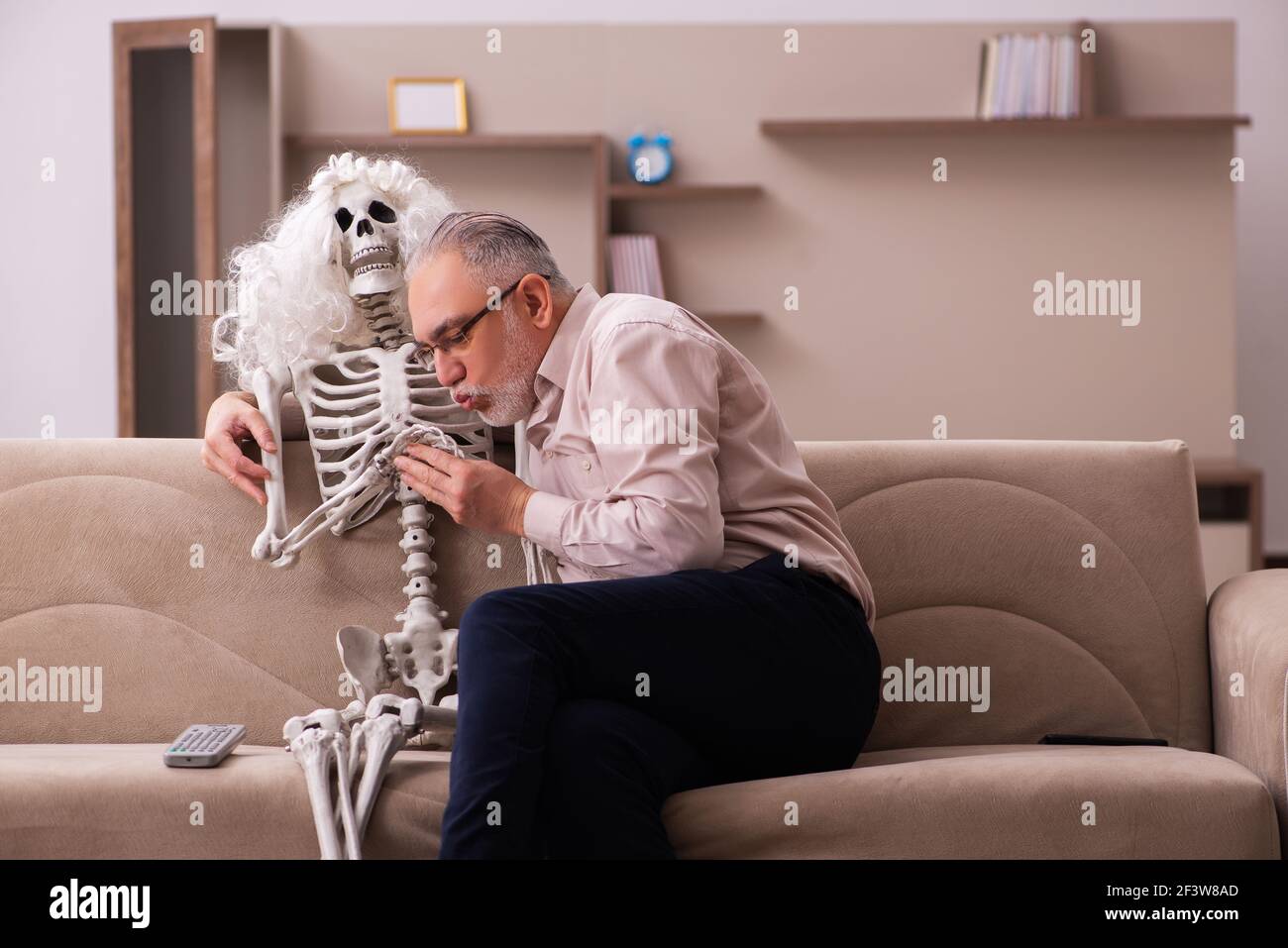 Old man sitting on the sofa with the female skeleton in undying love ...