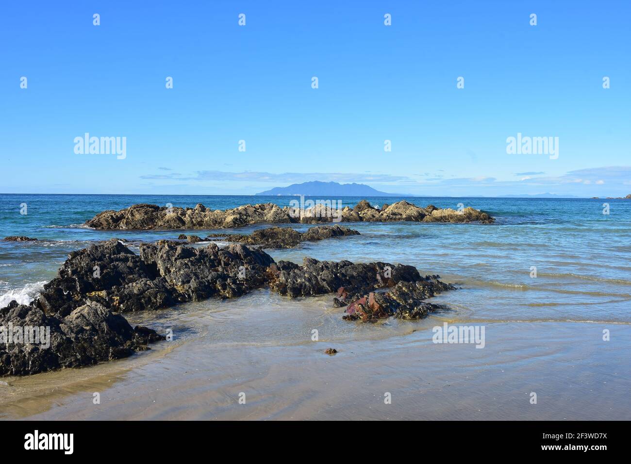 Flat formation of dark rocks exposed on sandy beach during low tide ...