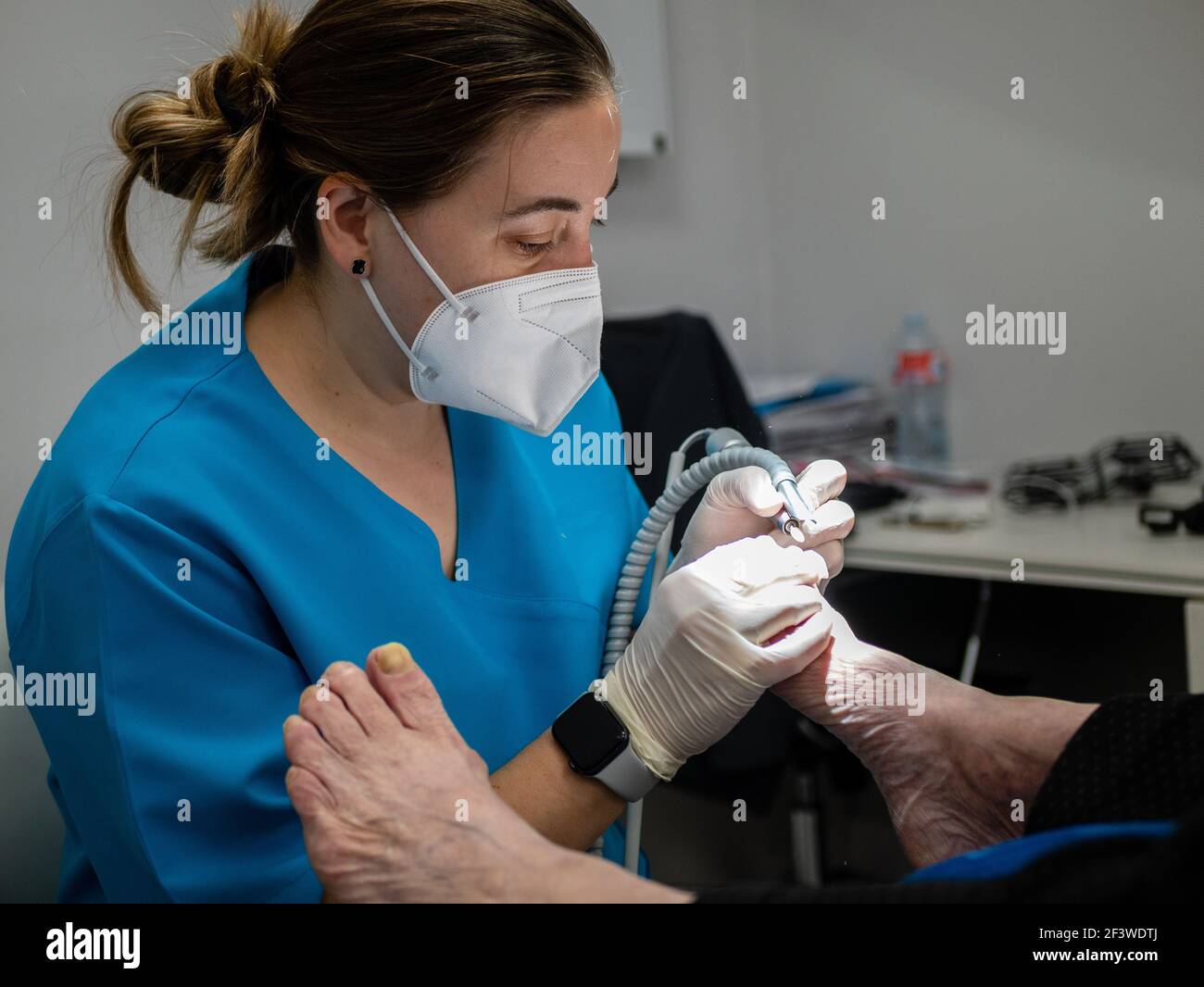 A female Caucasian podiatrist with a mask in her clinic, treating the ...