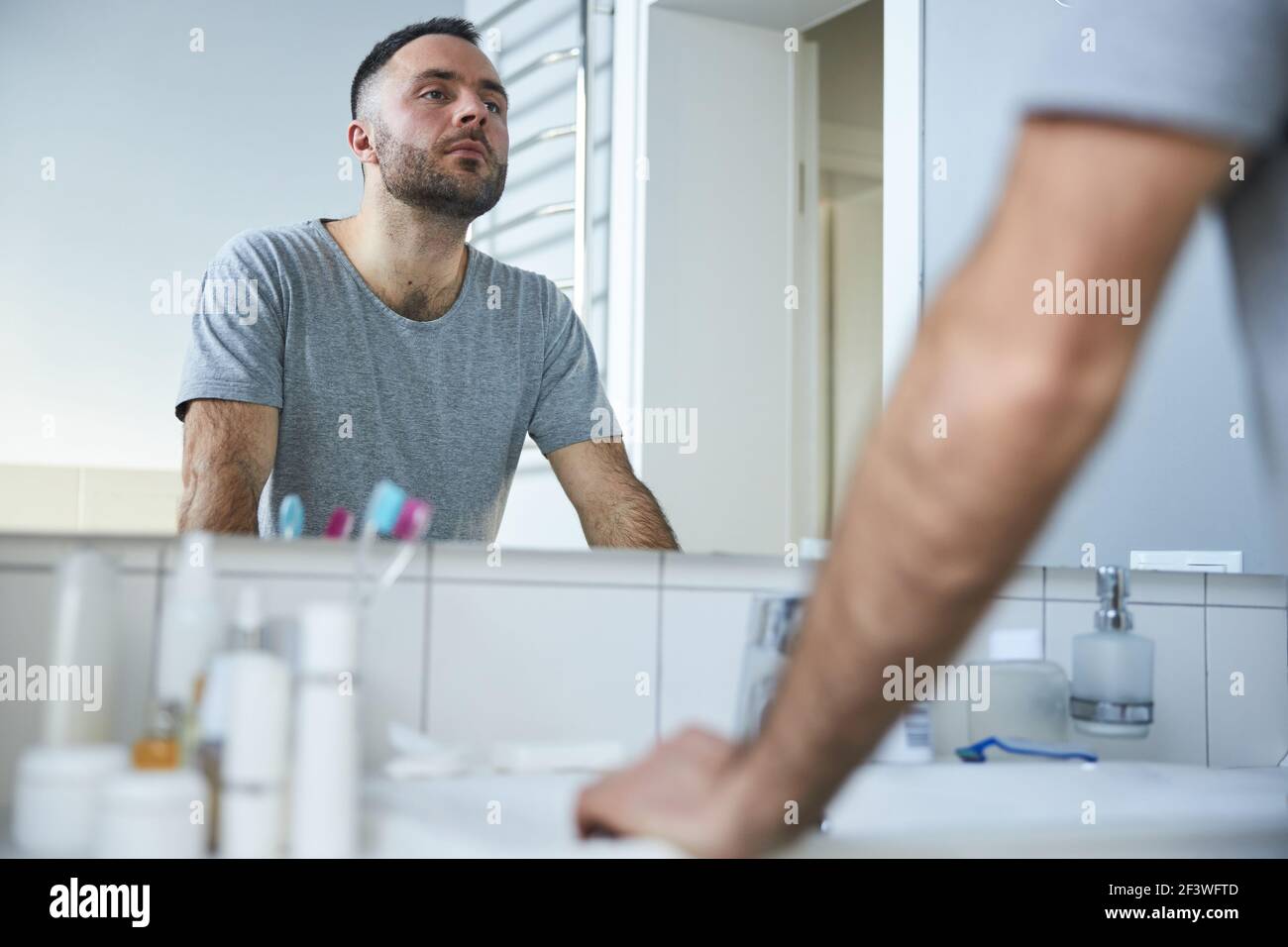 Attractive young man looking in the mirror in bathroom Stock Photo - Alamy