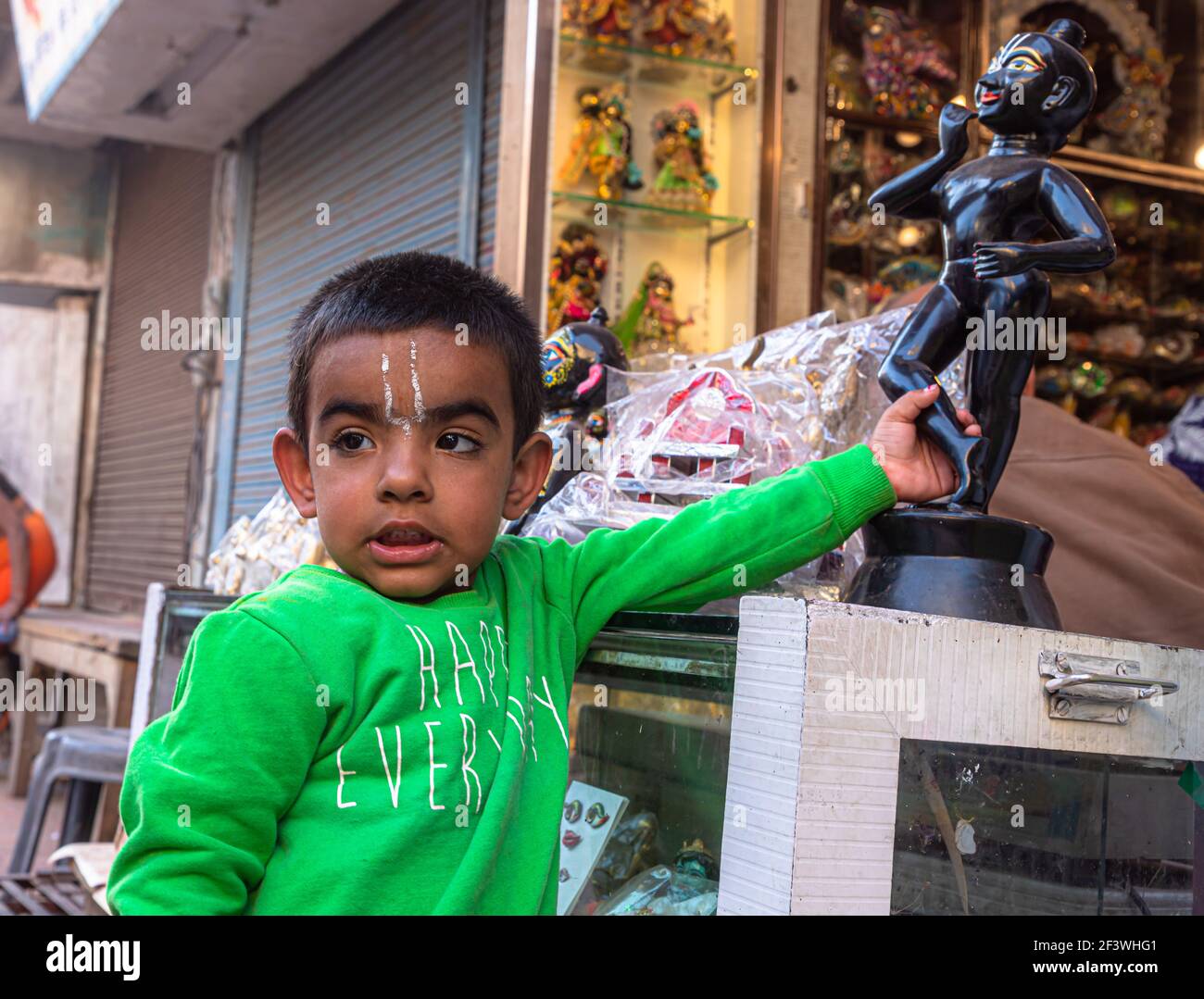a child holding krishna idol in streets of mathura with selective focus ...