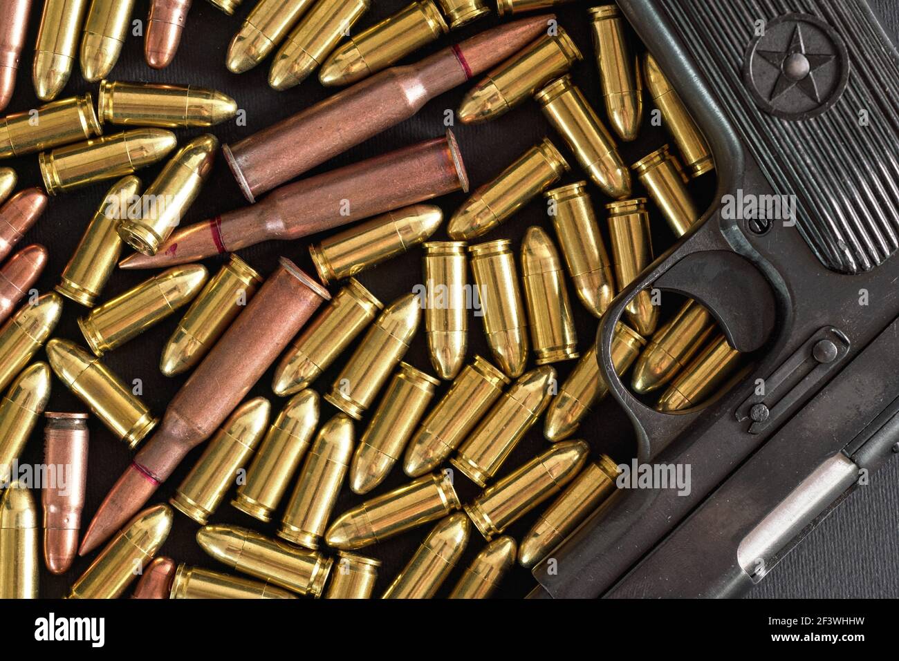 Yellow brass and brown bronze bullets, with black gun near, closeup ...