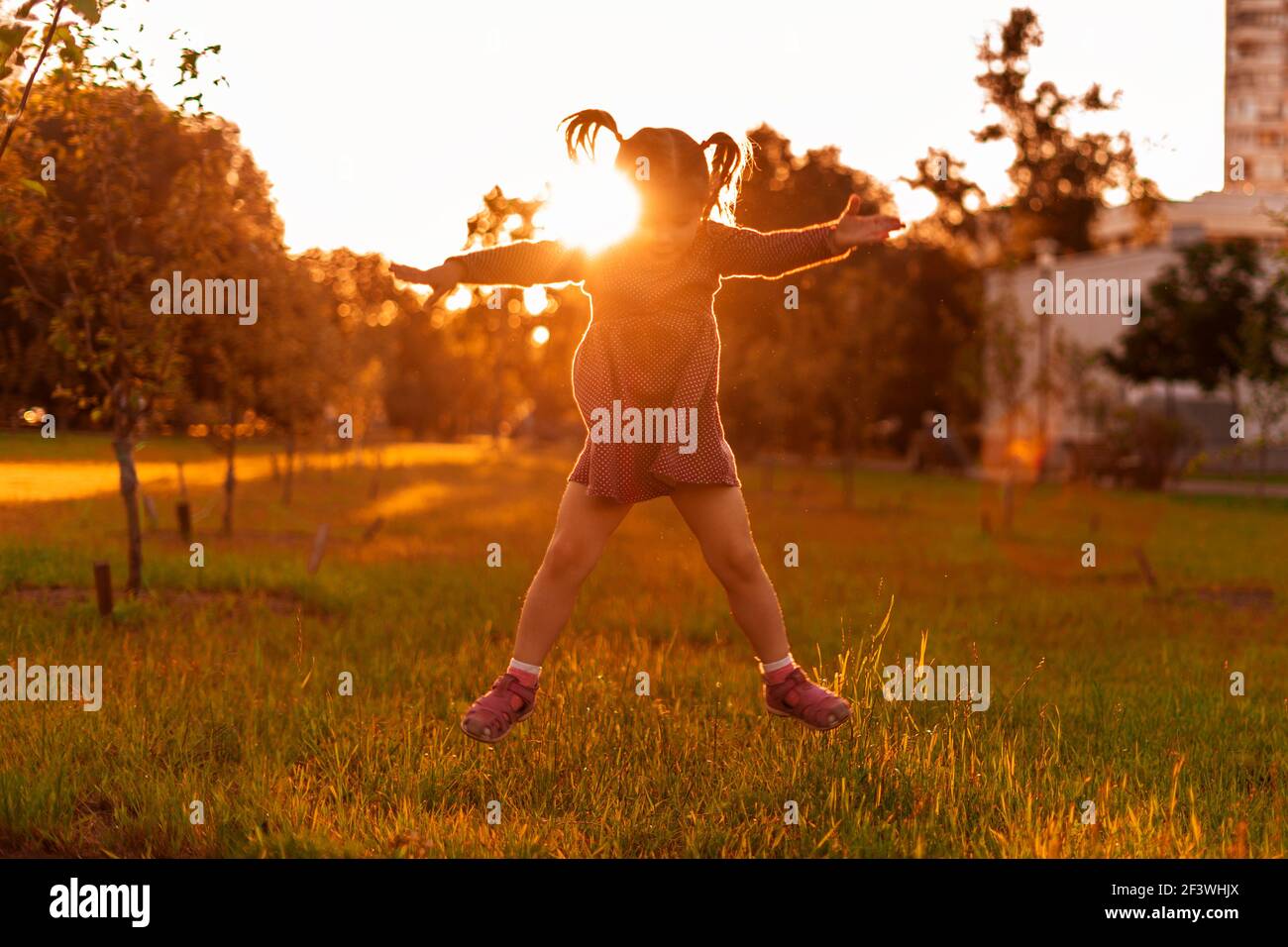cheerful little girl having fun and jumping at sunset in the evening ...